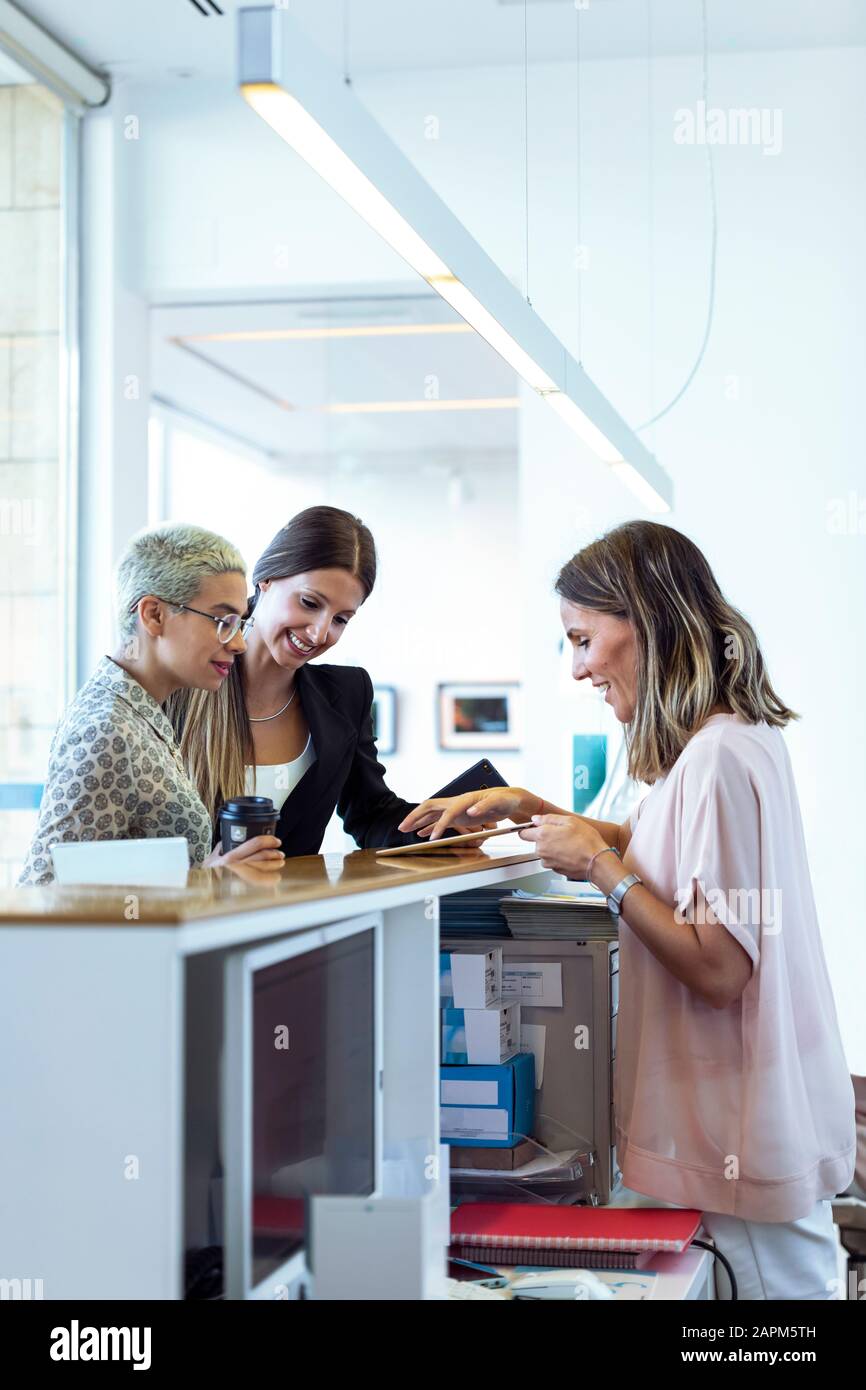 Two smiling businesswomen talking to woman at reception desk Stock ...