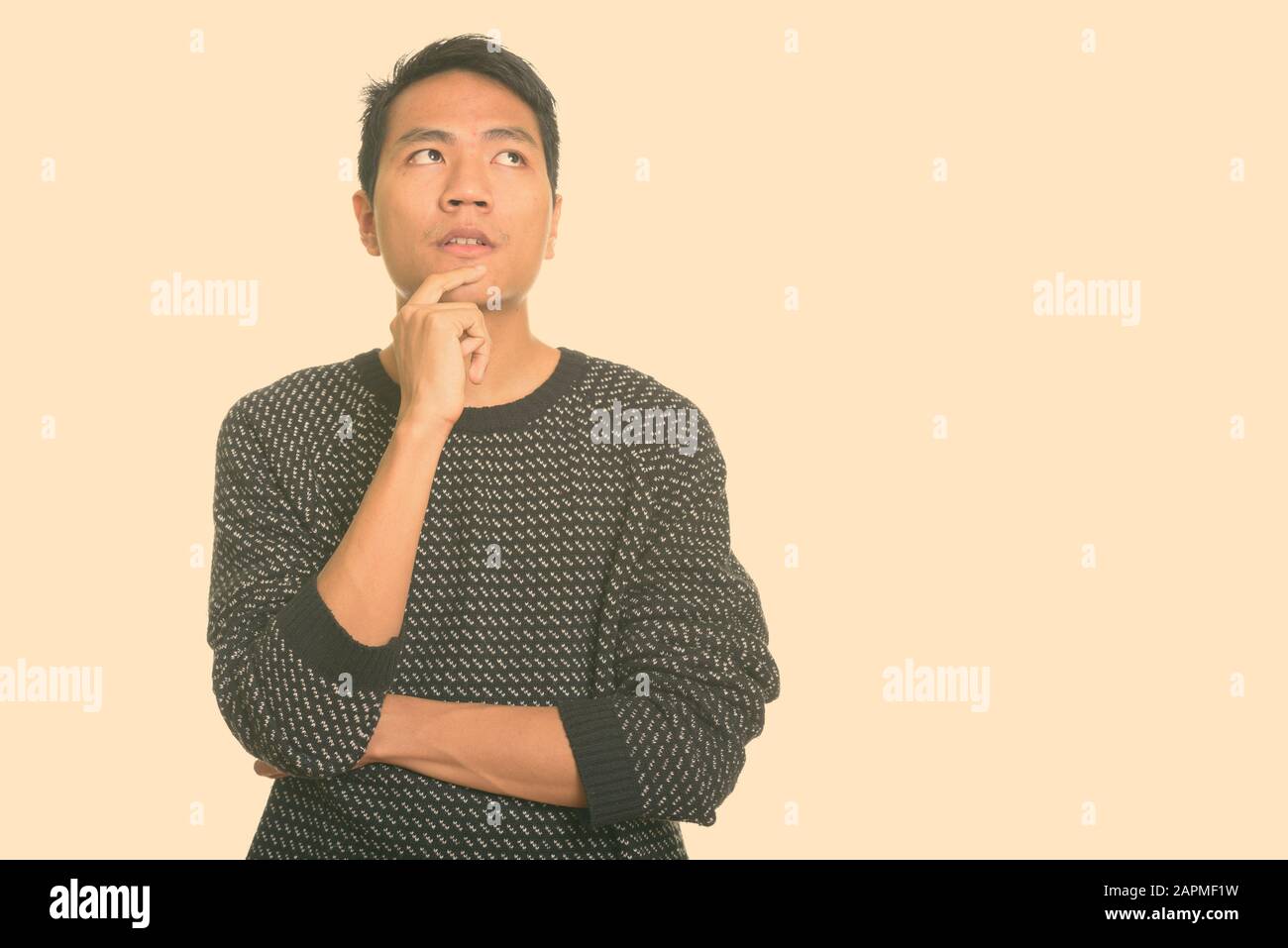 Studio shot of young Asian man thinking Stock Photo - Alamy