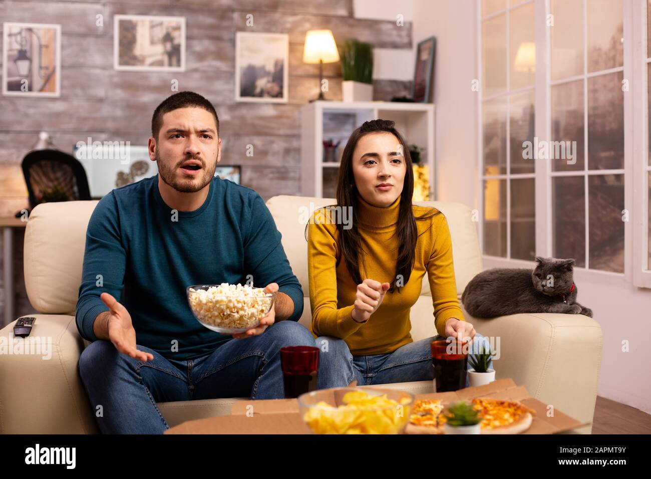 Couple cheering for their favourite team while watching TV and eating ...