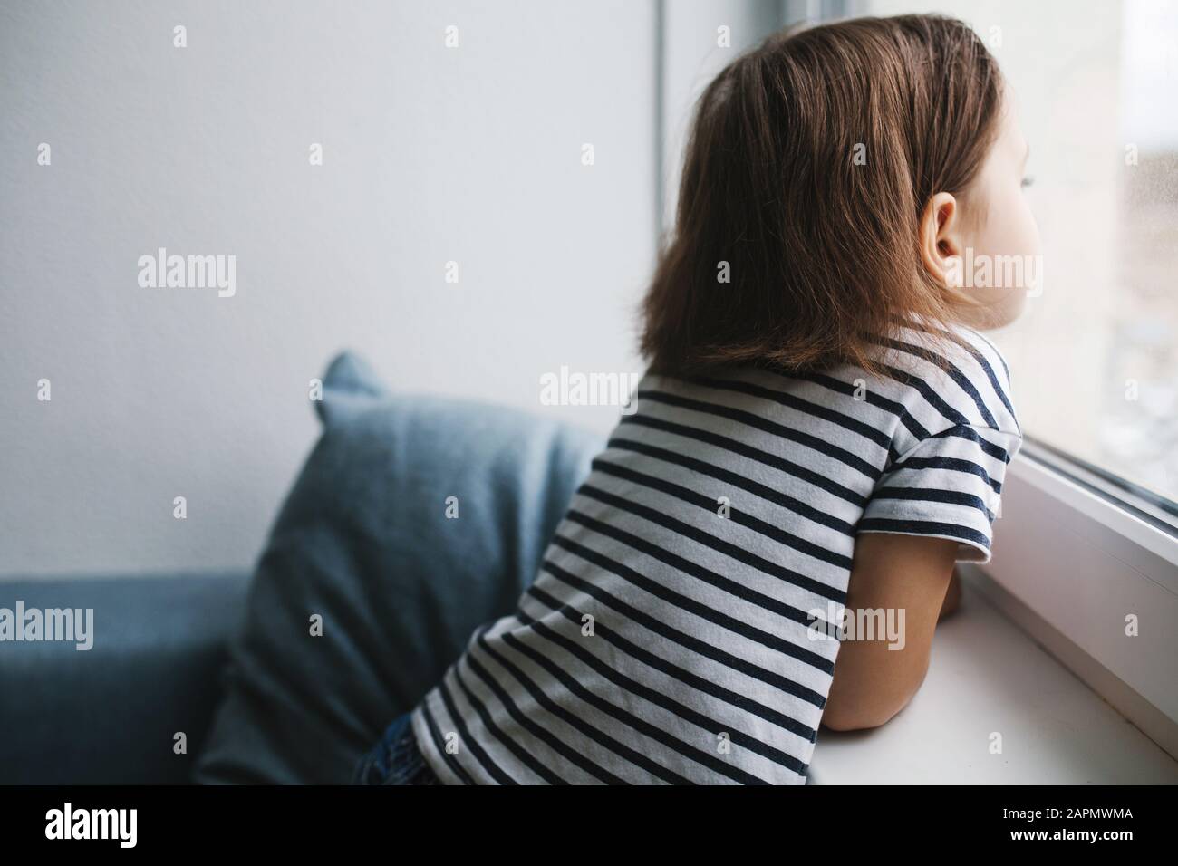 Little bored girl child sitting at home and looking at the window. Side ...