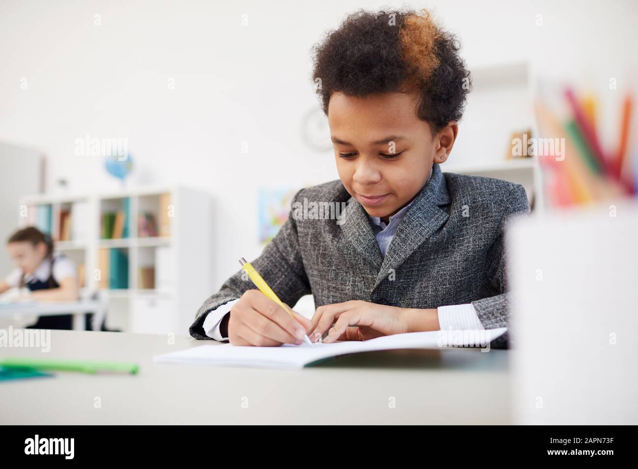 African boy sitting at desk and making notes in his notebook during ...