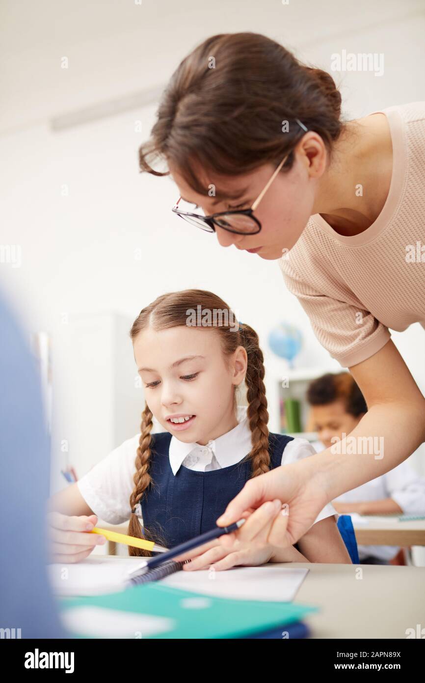 Young teacher helping the schoolgirl with task she pointing at notebook ...