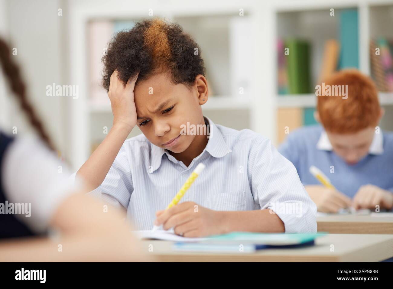 African pensive schoolboy sitting at desk and concentrating on his task ...