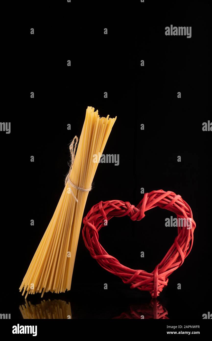 Wicker red heart and flying bunch of raw dry spaghetti on black ...