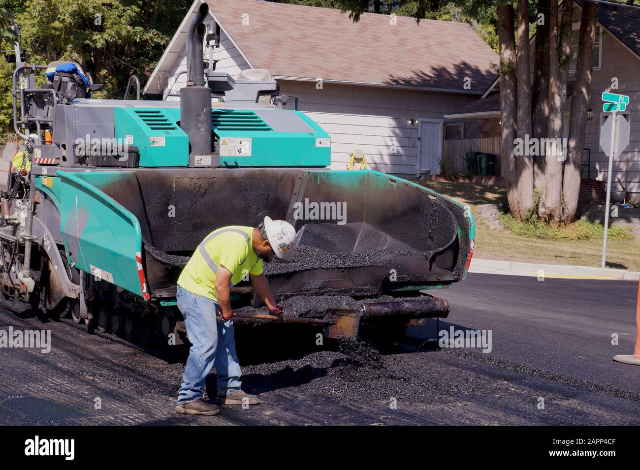The worker uses a shovel to spread hot asphalt on the road of the ...