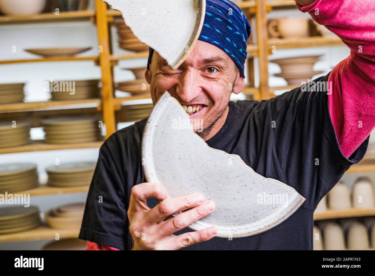 Funny potter smiling through the broken ceramic hand made plates in his ...
