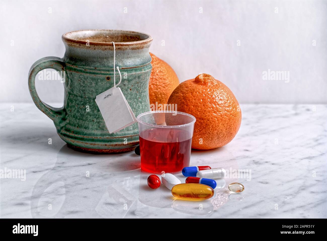 A green teacup, oranges, red cough syrup, and assorted pills are ...