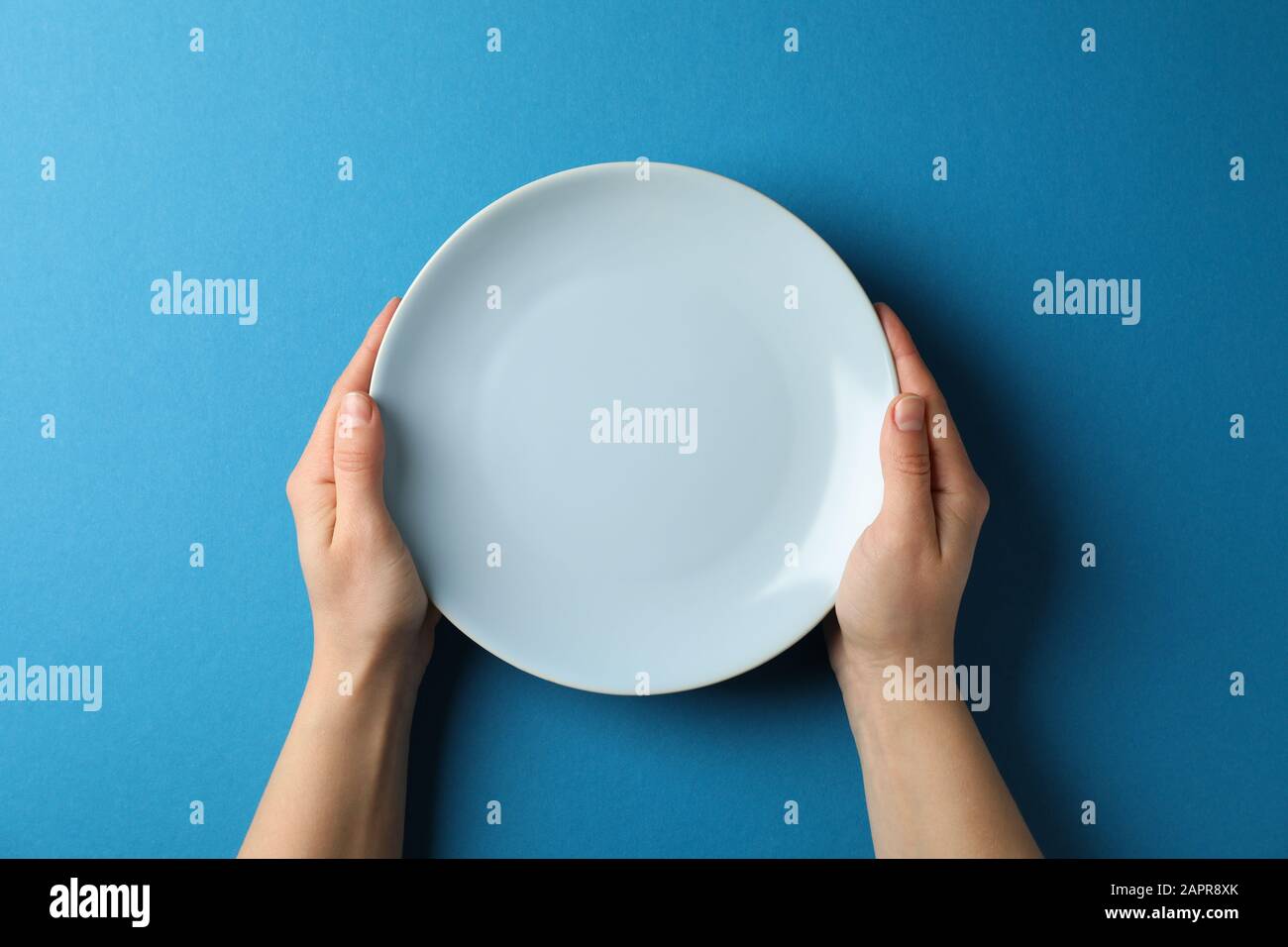 Female hands hold plate on blue background, top view Stock Photo - Alamy