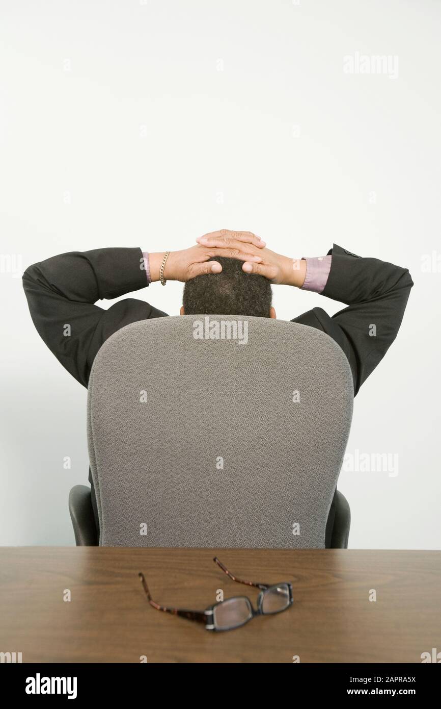 Rear view of a businessman sitting on an office chair with his hands ...