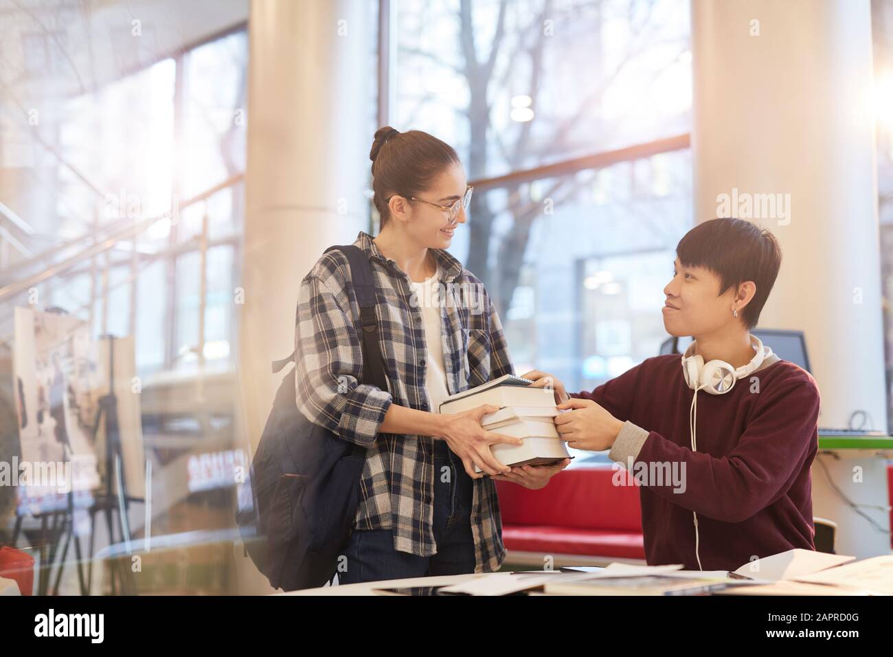 Young woman bringing heap of books for her friend and they are going to ...