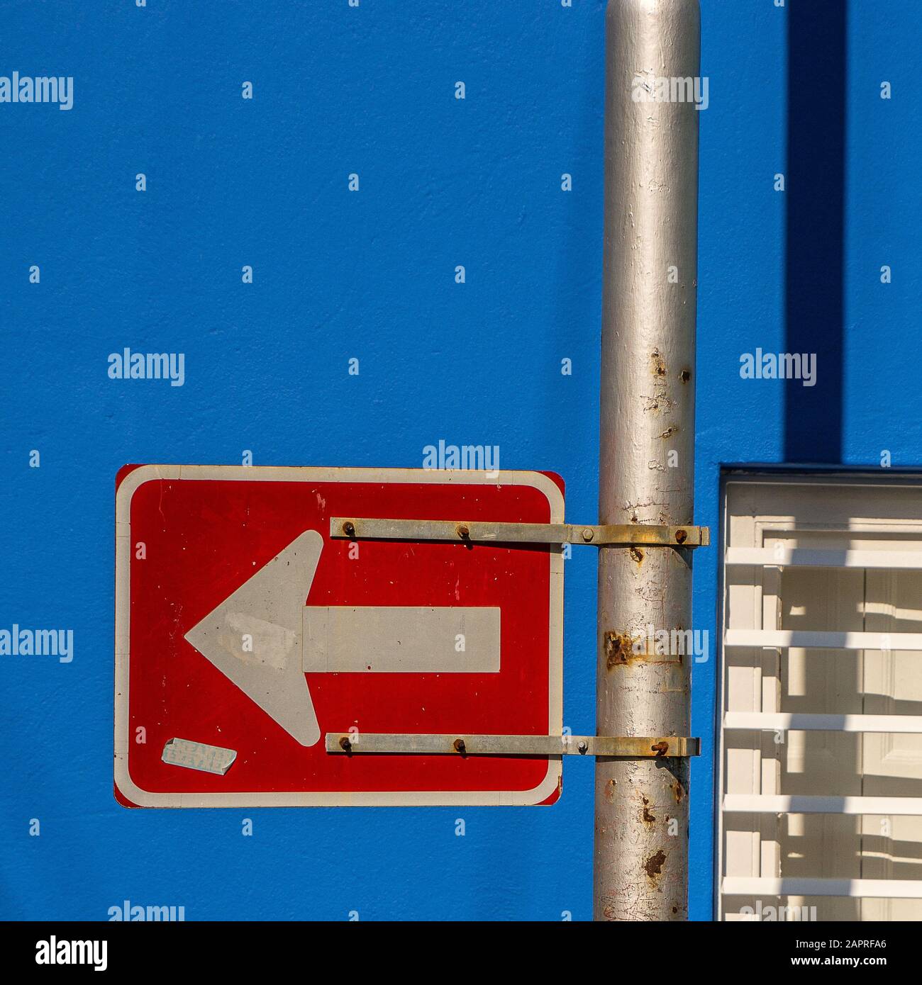 Arrow on a red sign attached to a metal pole behind a blue background ...