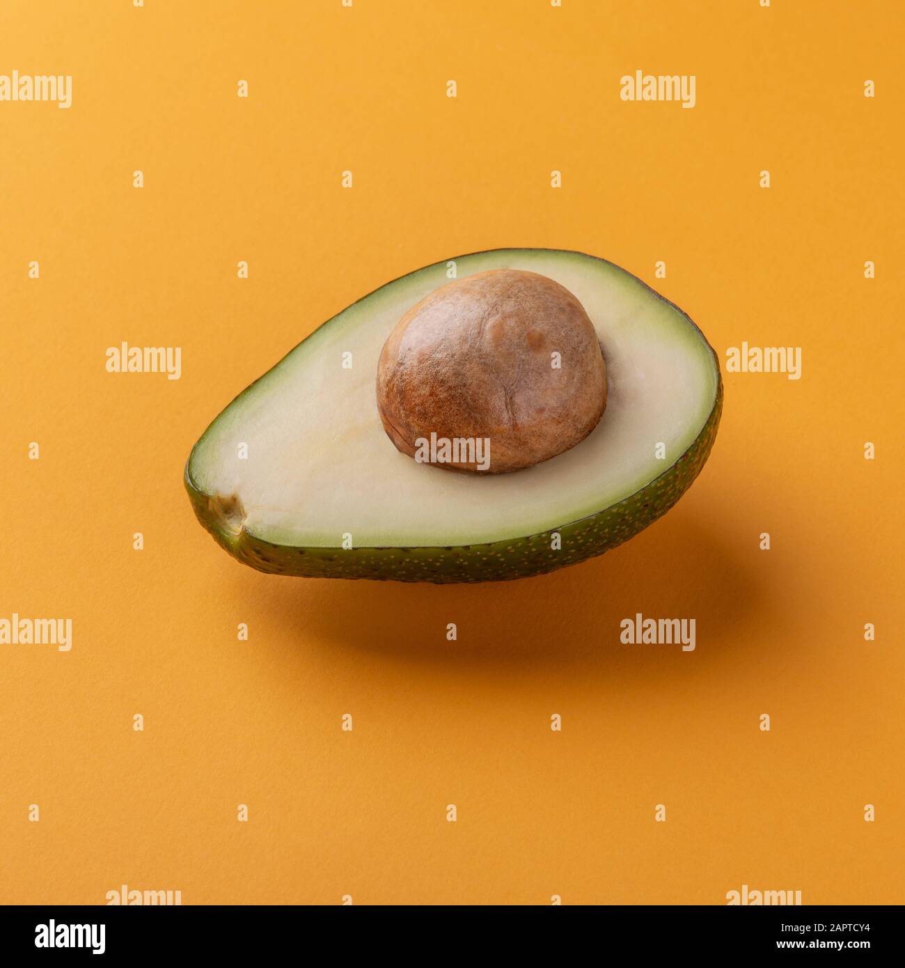 Avocado half with kernel on orange background Stock Photo - Alamy