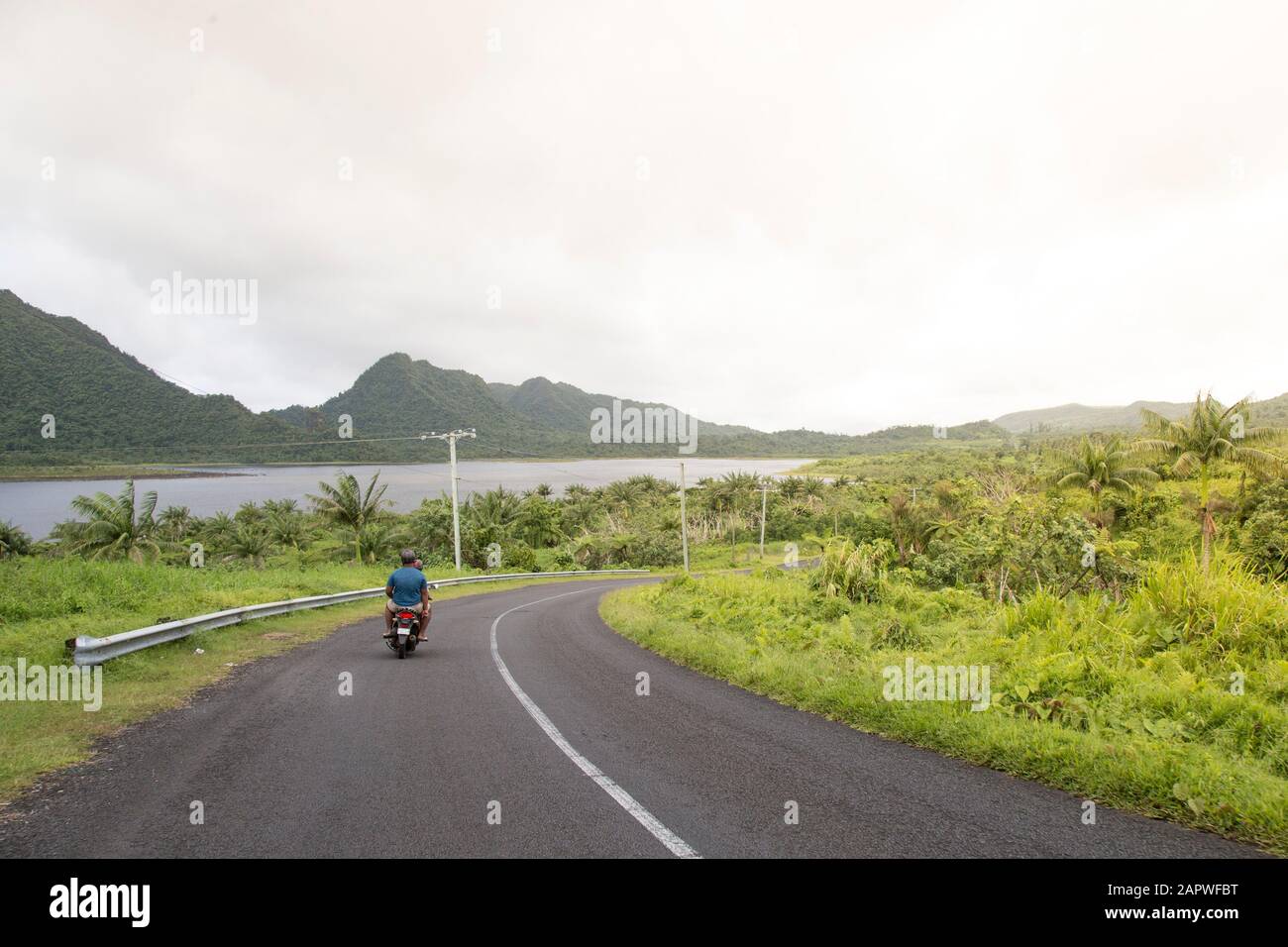 Two people riding a scooter across an exotic and tropical landscape ...