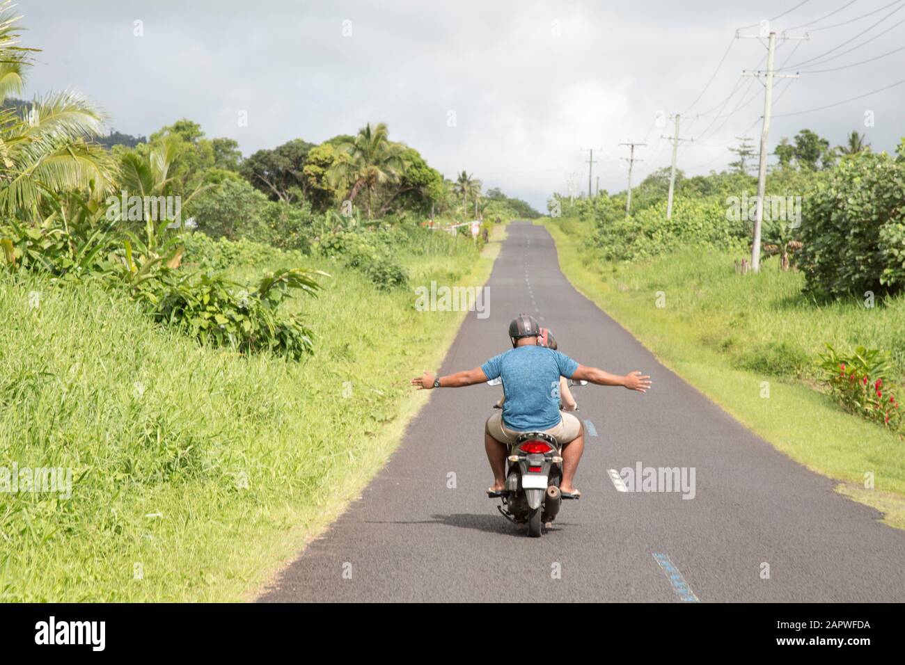 Two people riding a scooter across an exotic and tropical landscape ...