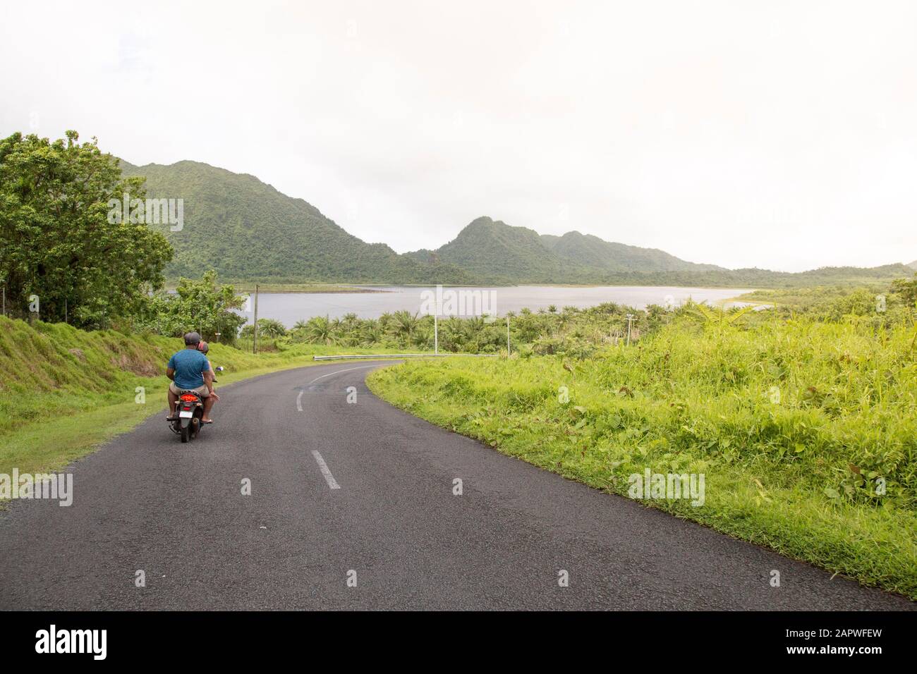 Two people riding a scooter across an exotic and tropical landscape ...