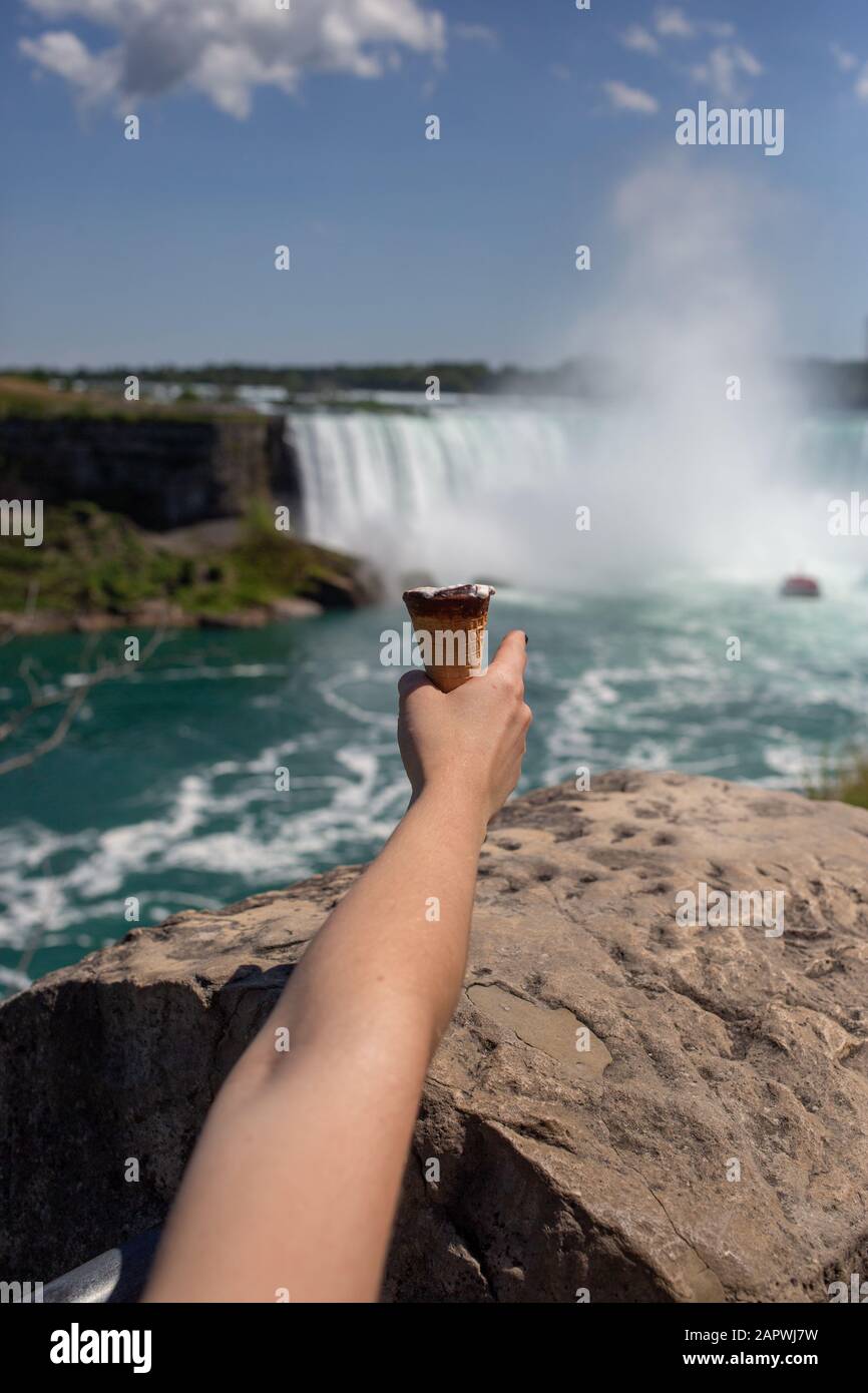Vertical shot of a girl holding ice cream with the view of a waterfall ...