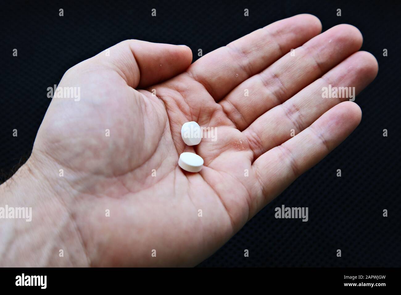 High angle shot of a person holding two white pills over a black ...