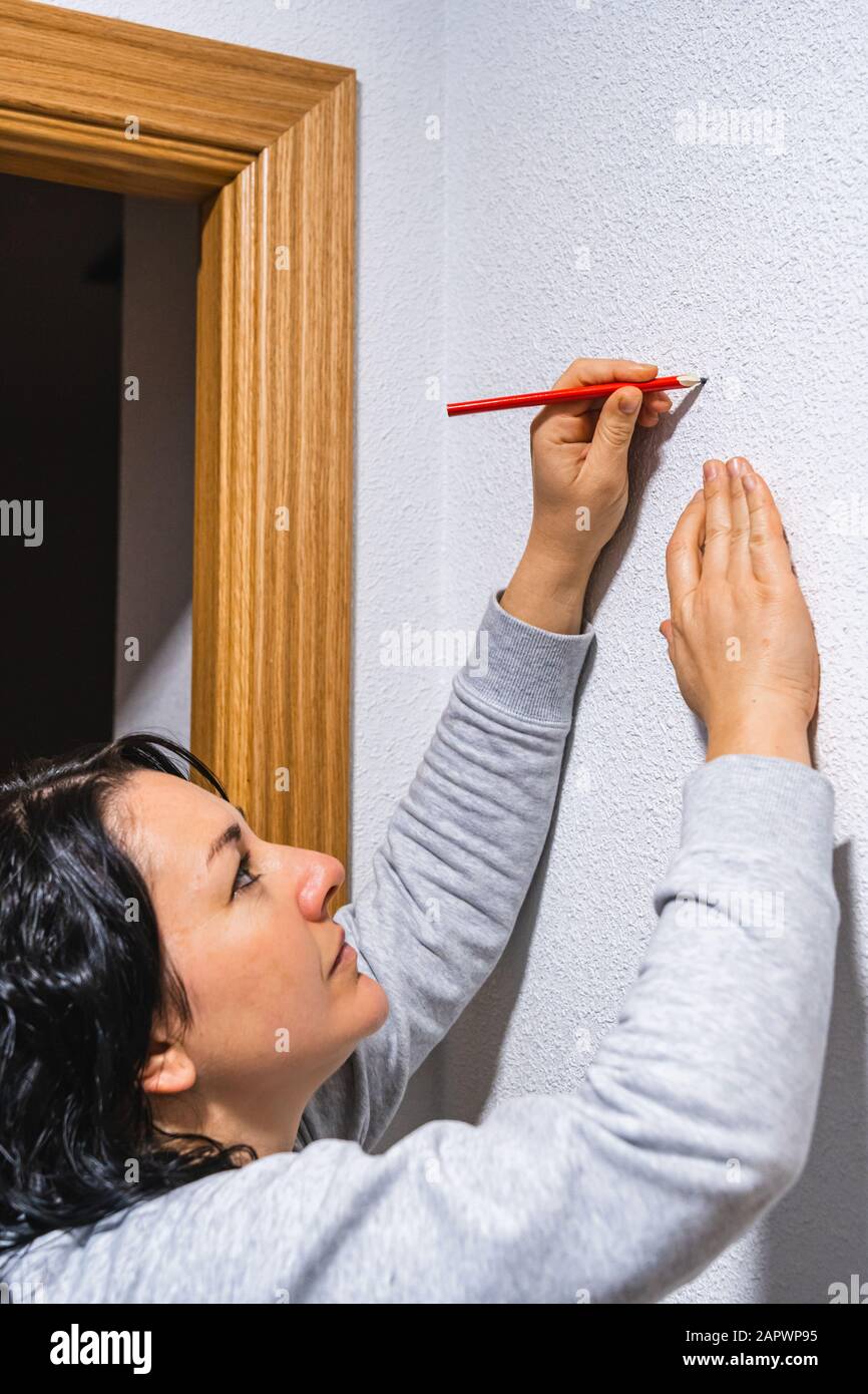 A smiling woman marking the white wall with a red carpenter's pencil ...