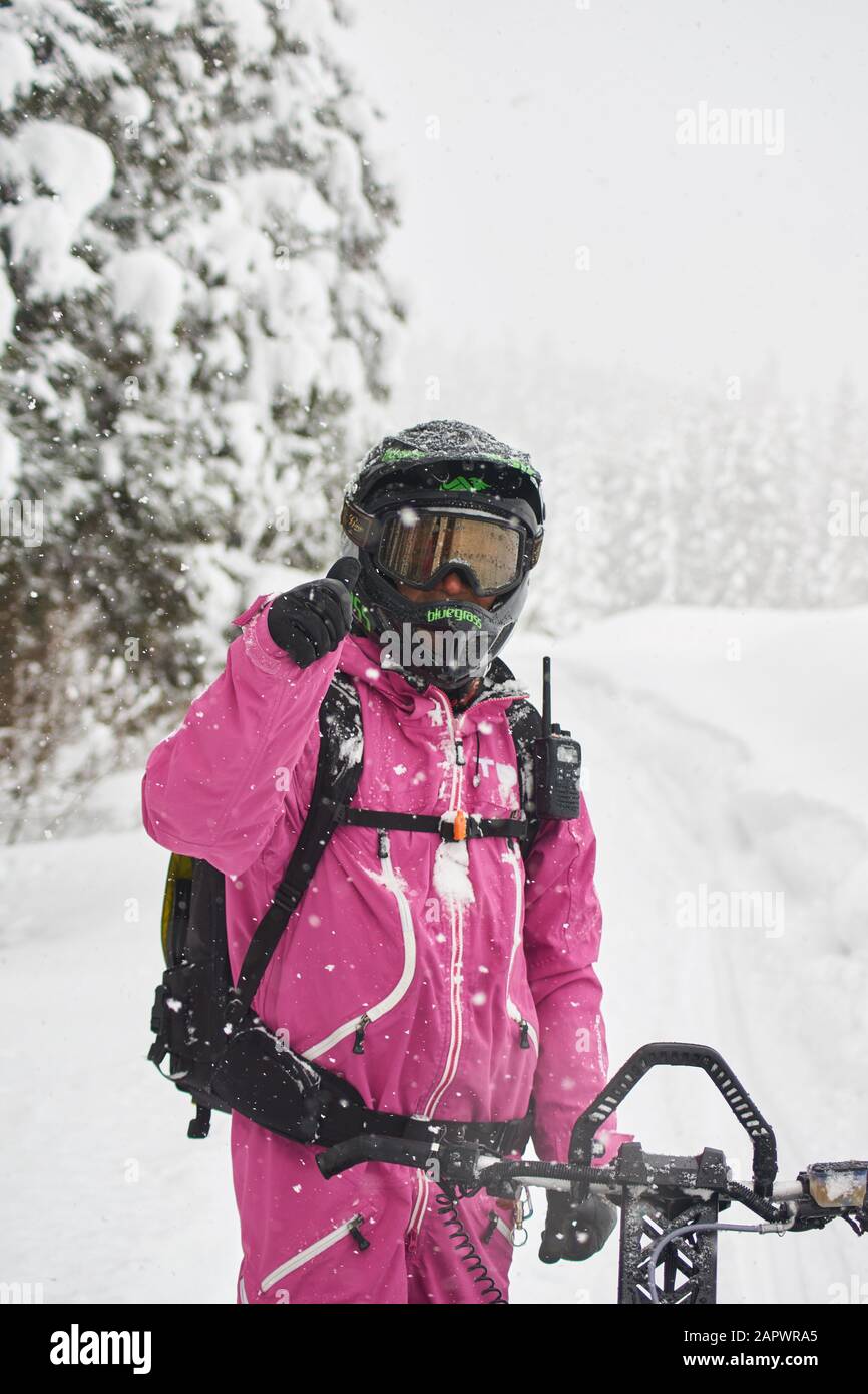 A man in a bright pink jacket and helmet stands on a snowmobile (snow ...