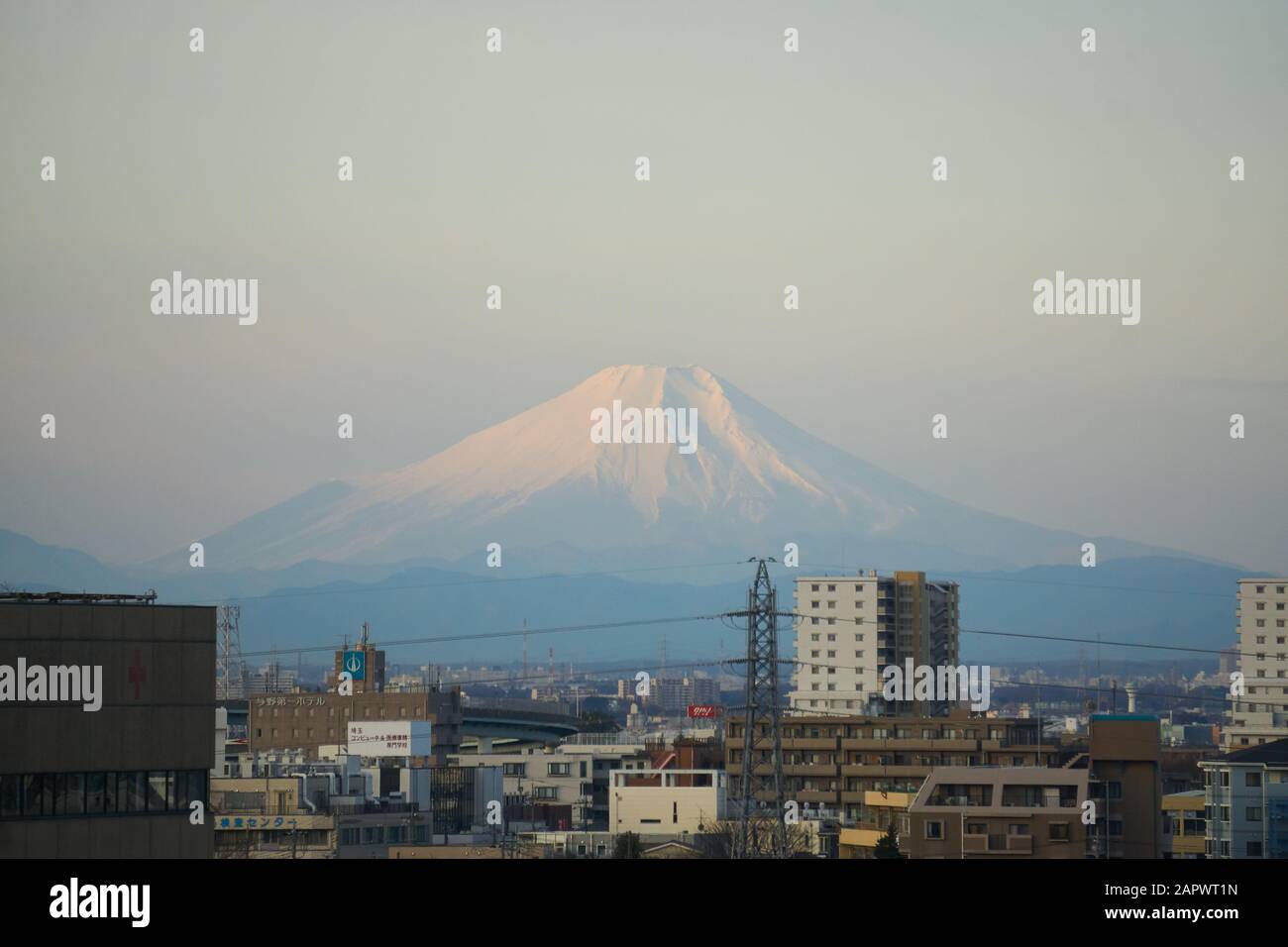 A snowy Mount Fuji (Mt. Fuji) towers in the distance over a city ...