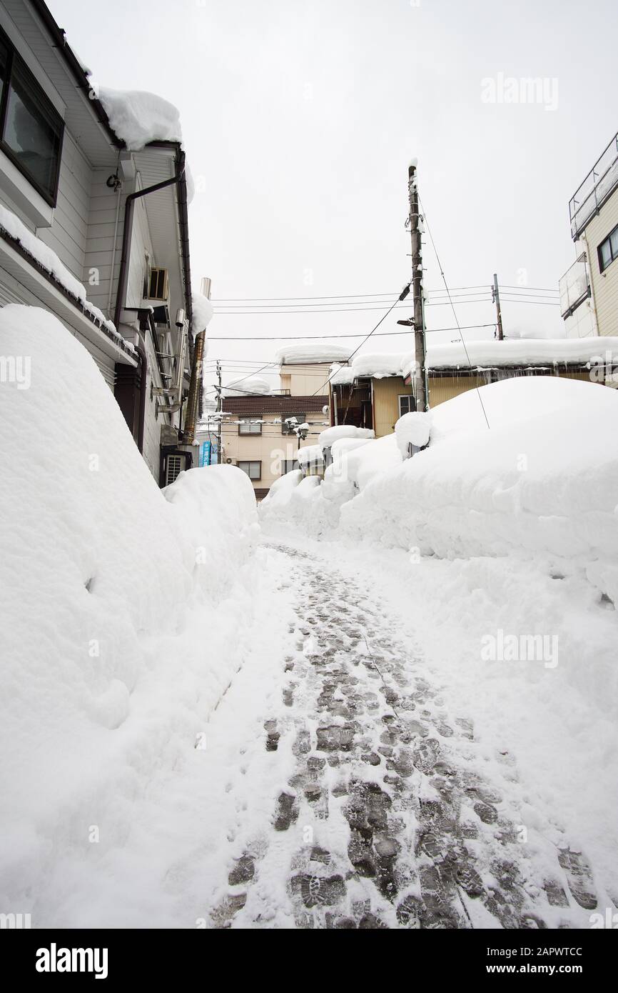 Snow is piled high on the sides of a sidewalk in Echigo-Yuzawa, Niigata ...
