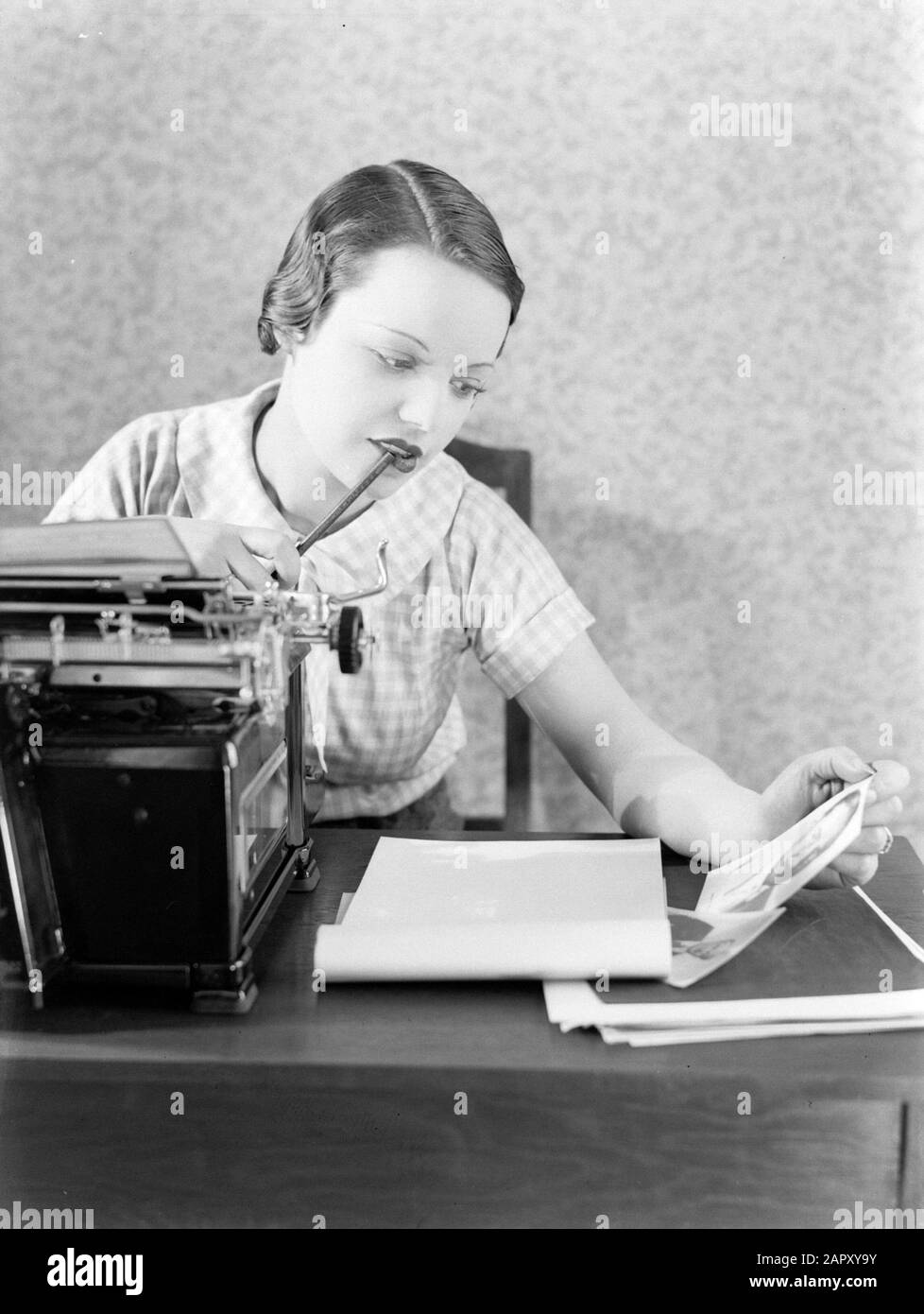 Woman behind a typewriter viewing a photo Date: 1931 Keywords ...