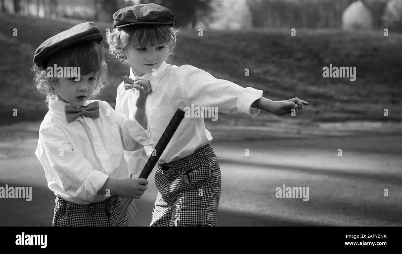 Greyscale of two kids with hats and bowties in a garden under the ...