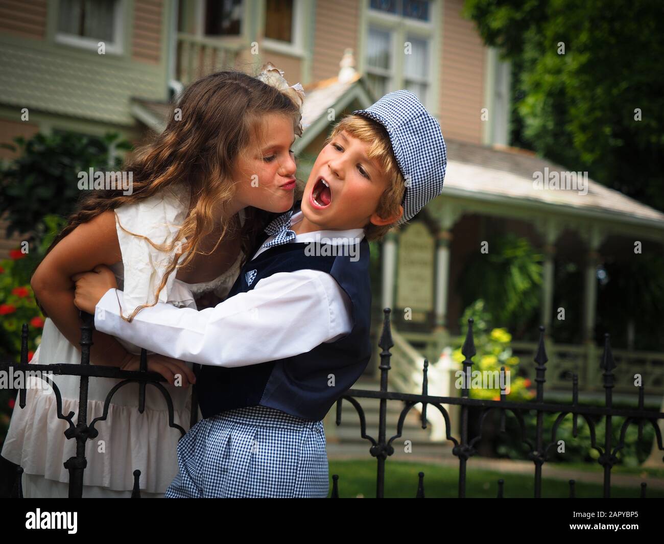 Adorable little girl trying to kiss a boy near a fence during daytime ...