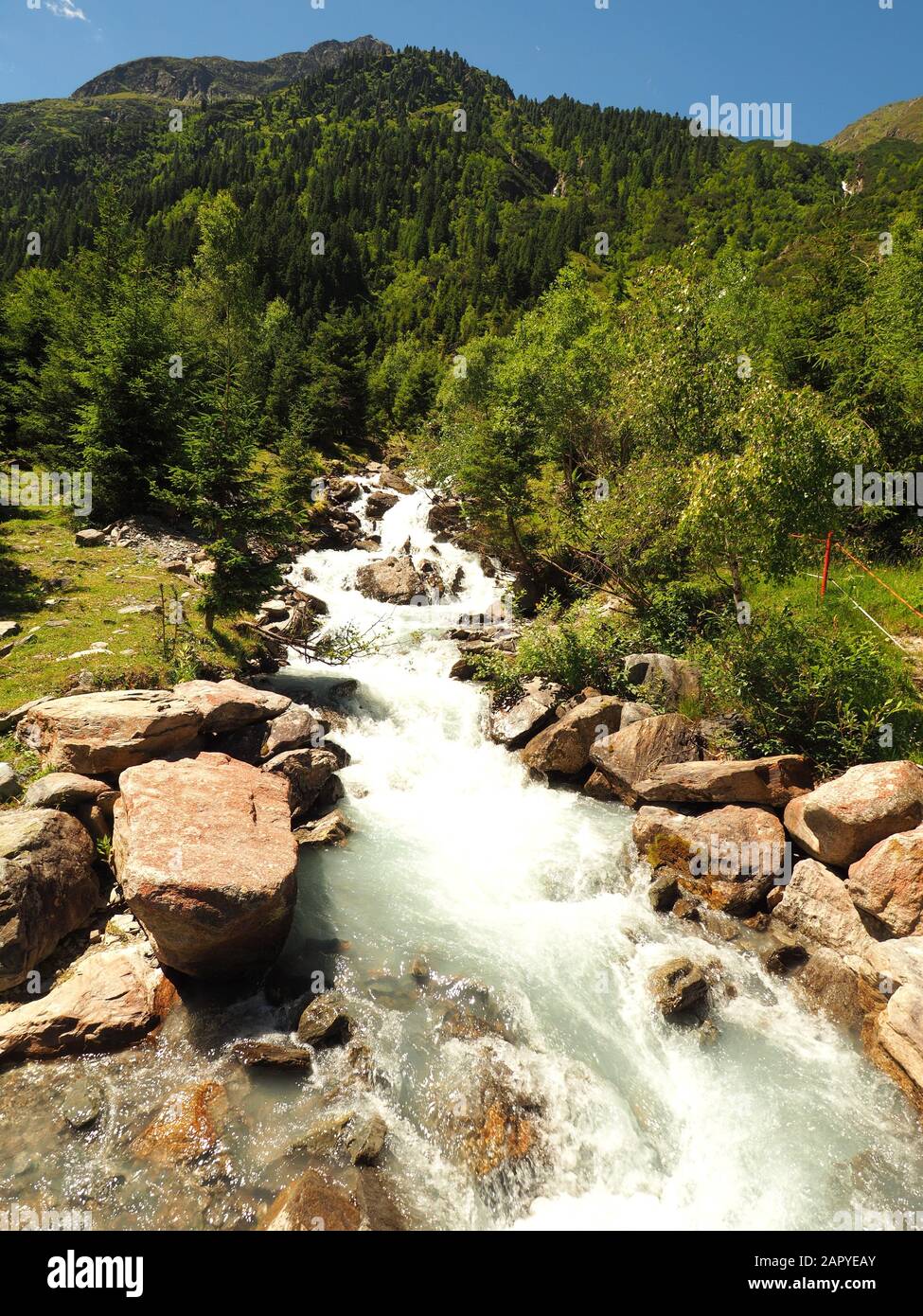 Vertical shot of stream water with green mountains, clear blue sky in ...