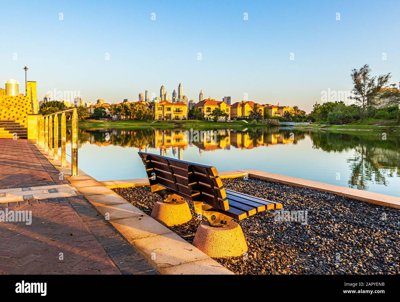 Bench on the shore of the lake with the reflections of buildings and ...