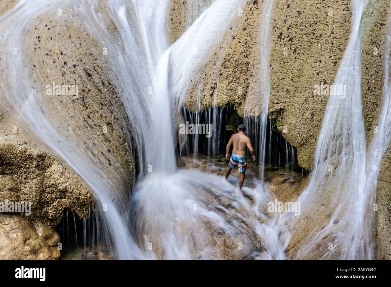 Man standing in shorts in a cave with water pouring down during the ...