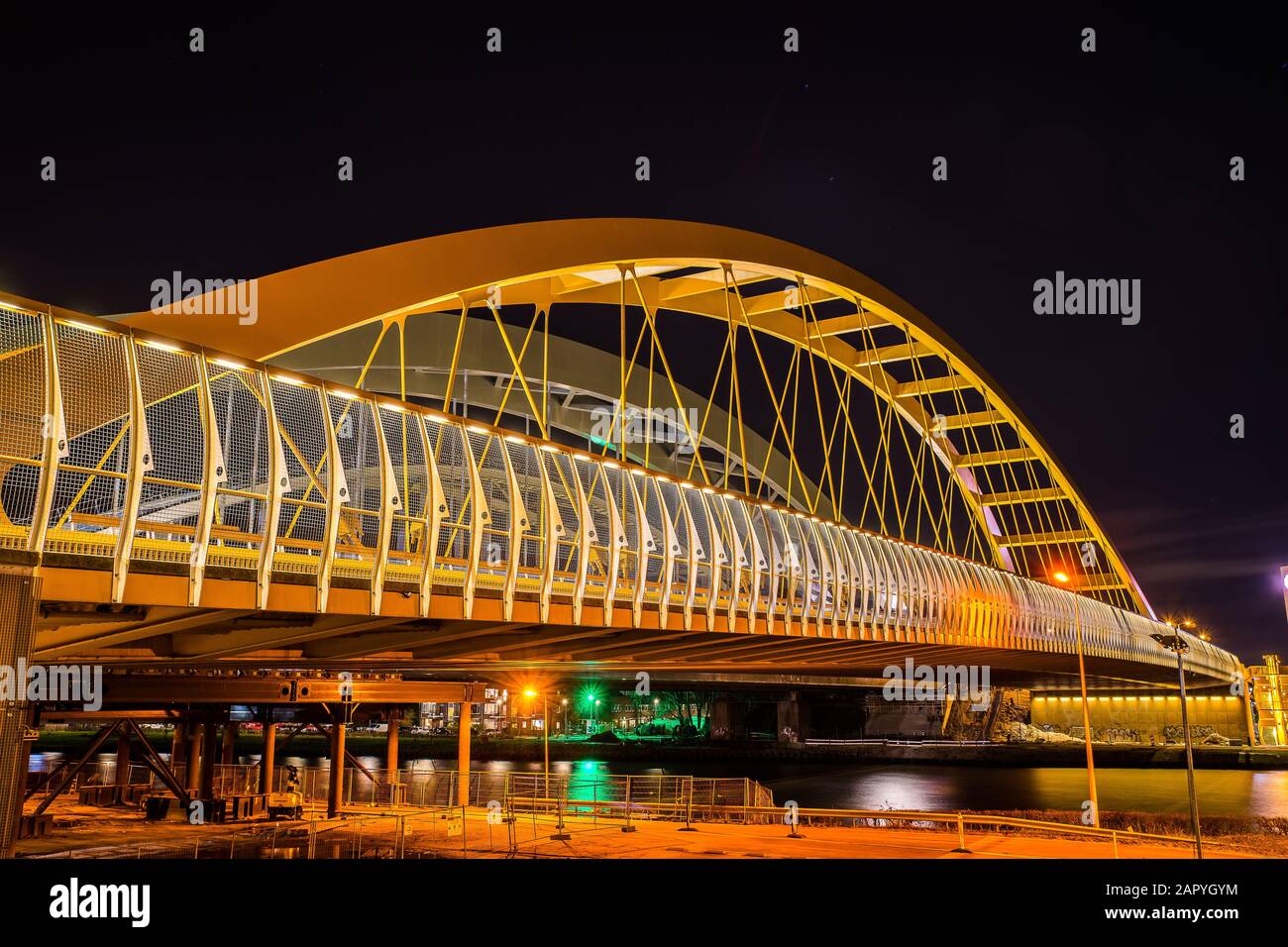 Bridge in a city with a large yellow arch on top at nighttime Stock ...