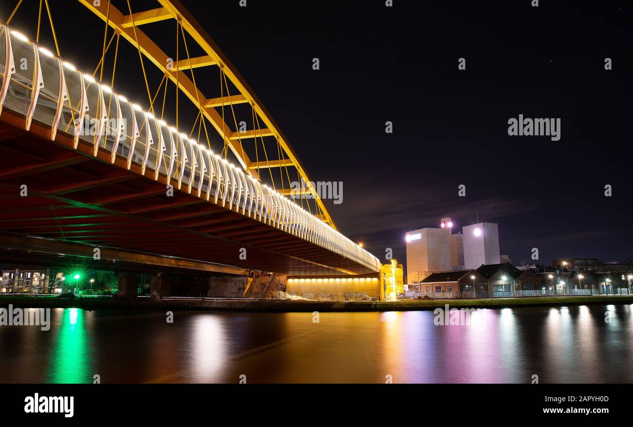 Bridge in a city with a large yellow arch on top at nighttime Stock ...