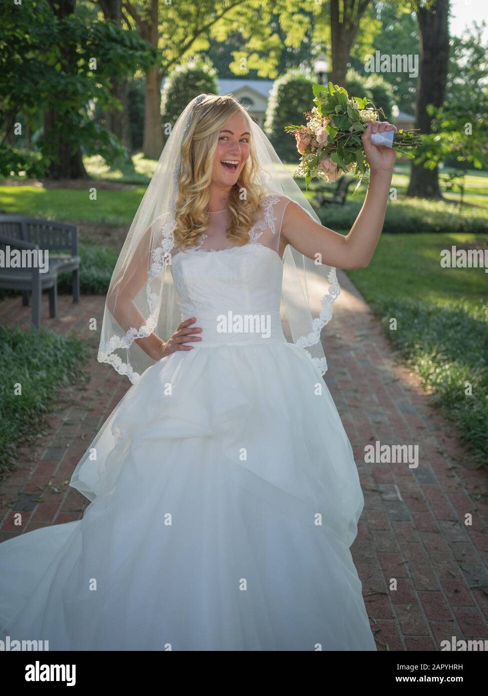 Vertical picture of a smiling bride with a bouquet in a garden under ...