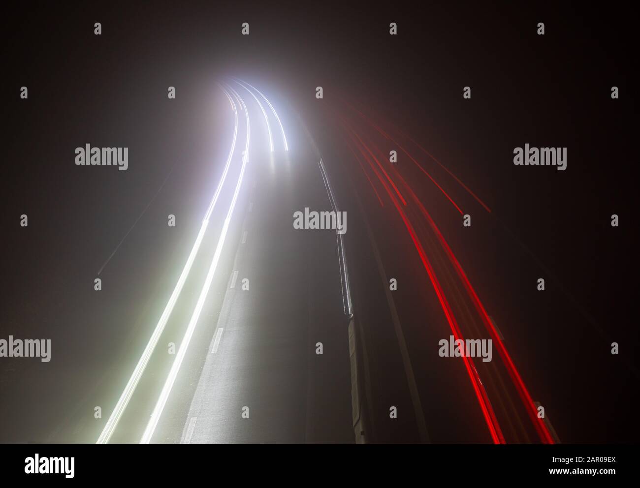 Highway at foggy night with bright trails of light from incoming and ...