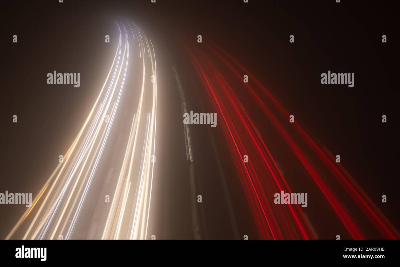 Highway at foggy night with bright trails of light from incoming and ...