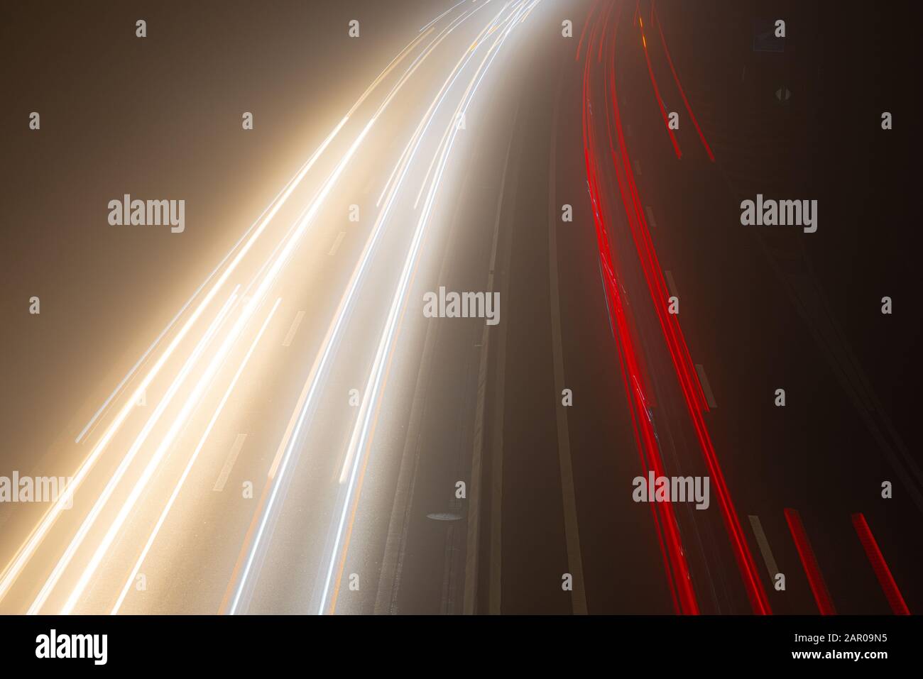 Highway at foggy night with bright trails of light from incoming and ...