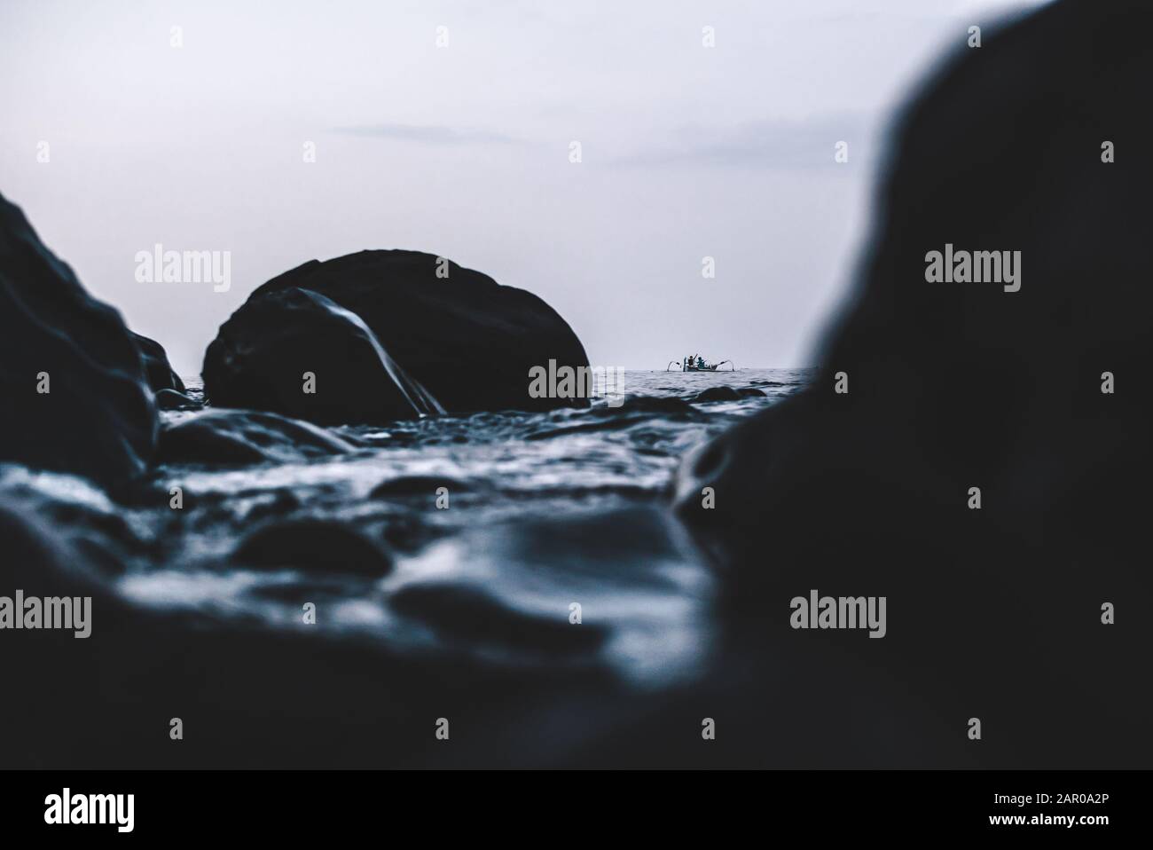 Small single boat in the distance and big rocks and water in the ...