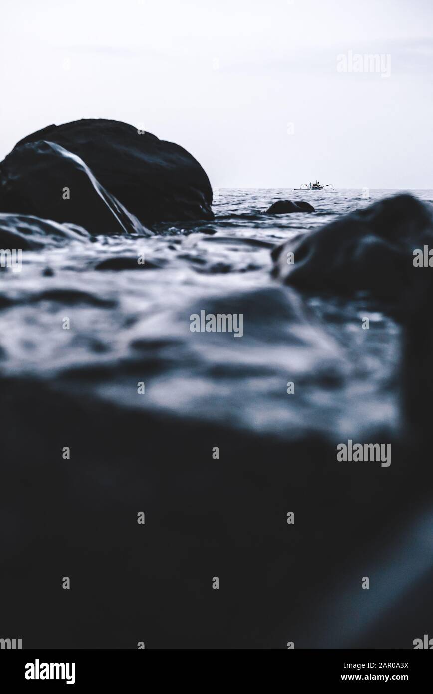 Small single boat in the distance and big rocks and water in the ...