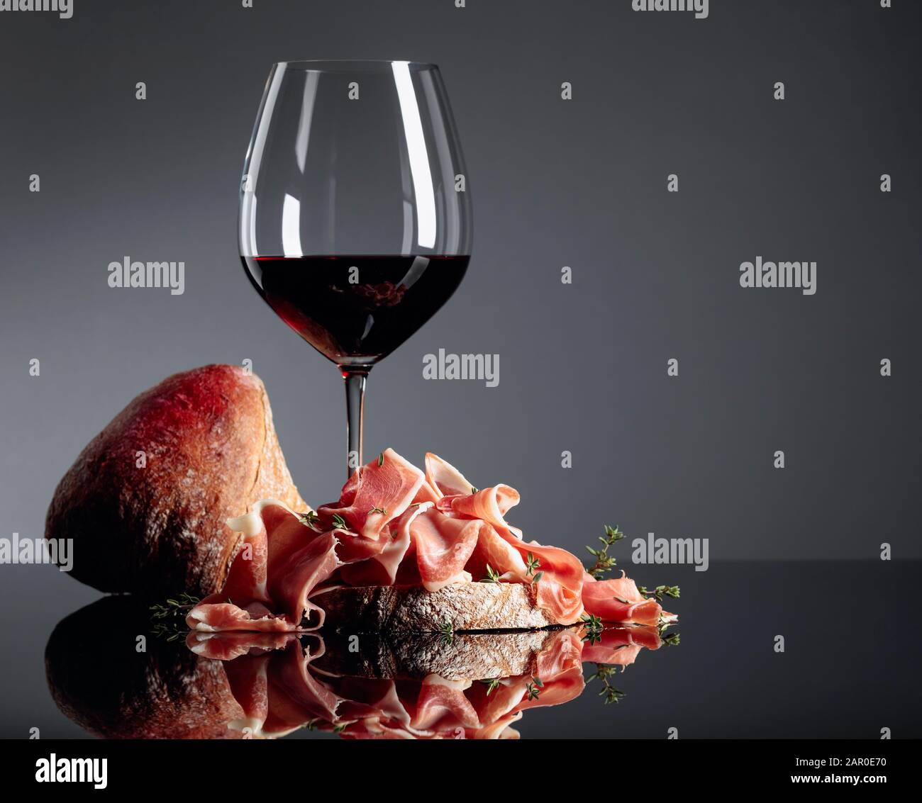 Prosciutto with ciabatta, red wine and thyme on a black reflective ...