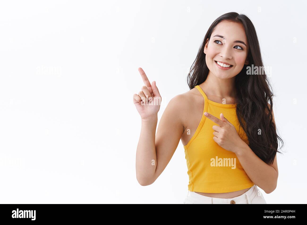 Dreamy pretty asian woman in stylish yellow top, gazing and pointing ...