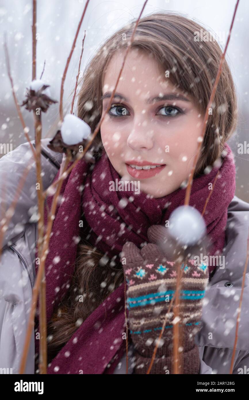 sad young woman freezes on winter meadow under falling snow looking at ...