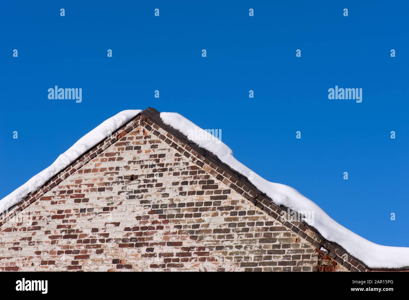 Brick wall and pediment of an old building against blue sky. Some snow ...