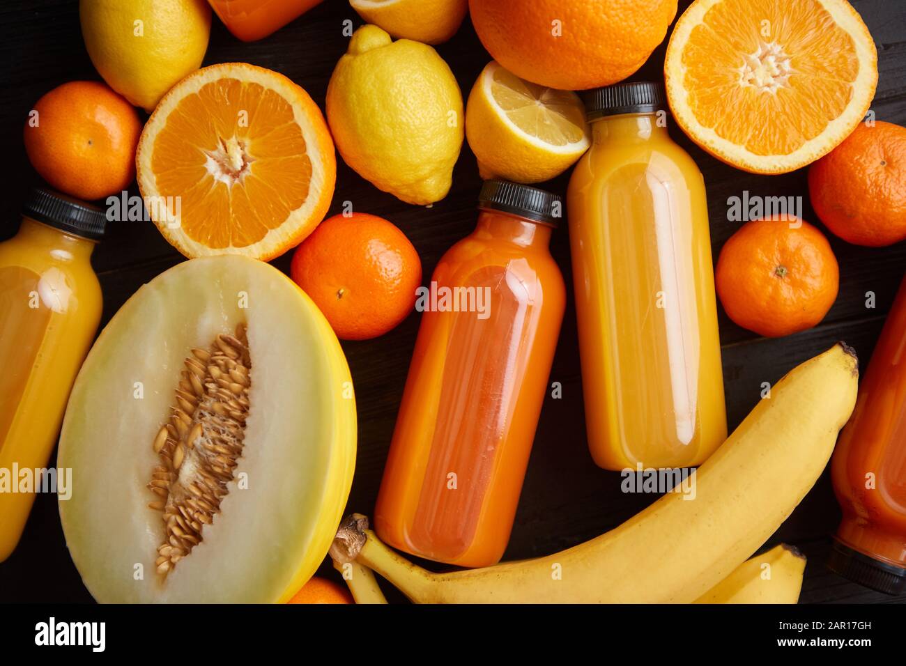 Mix of orange and yellow colored fruits and juices on black wooden ...