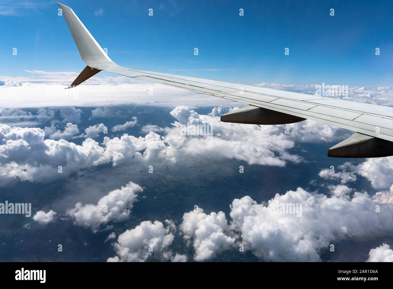 White clouds float under the wing of a sunlit airplane flying under a ...