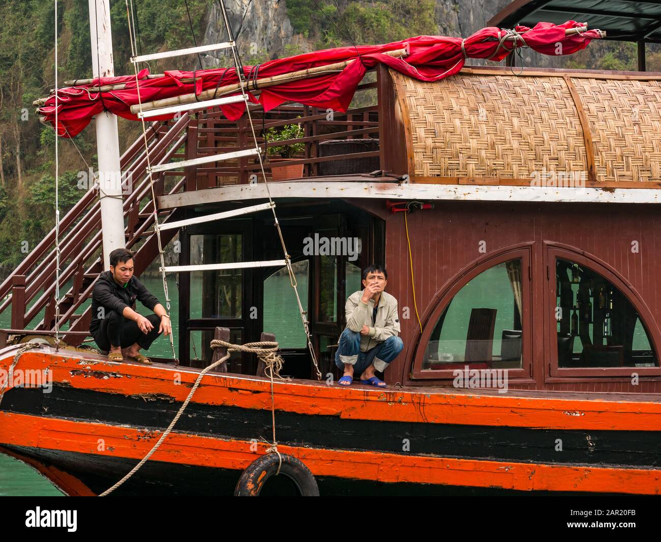 Asian men squatting and smoking on tourist boat, Cat Ba Island, Lan Ha ...