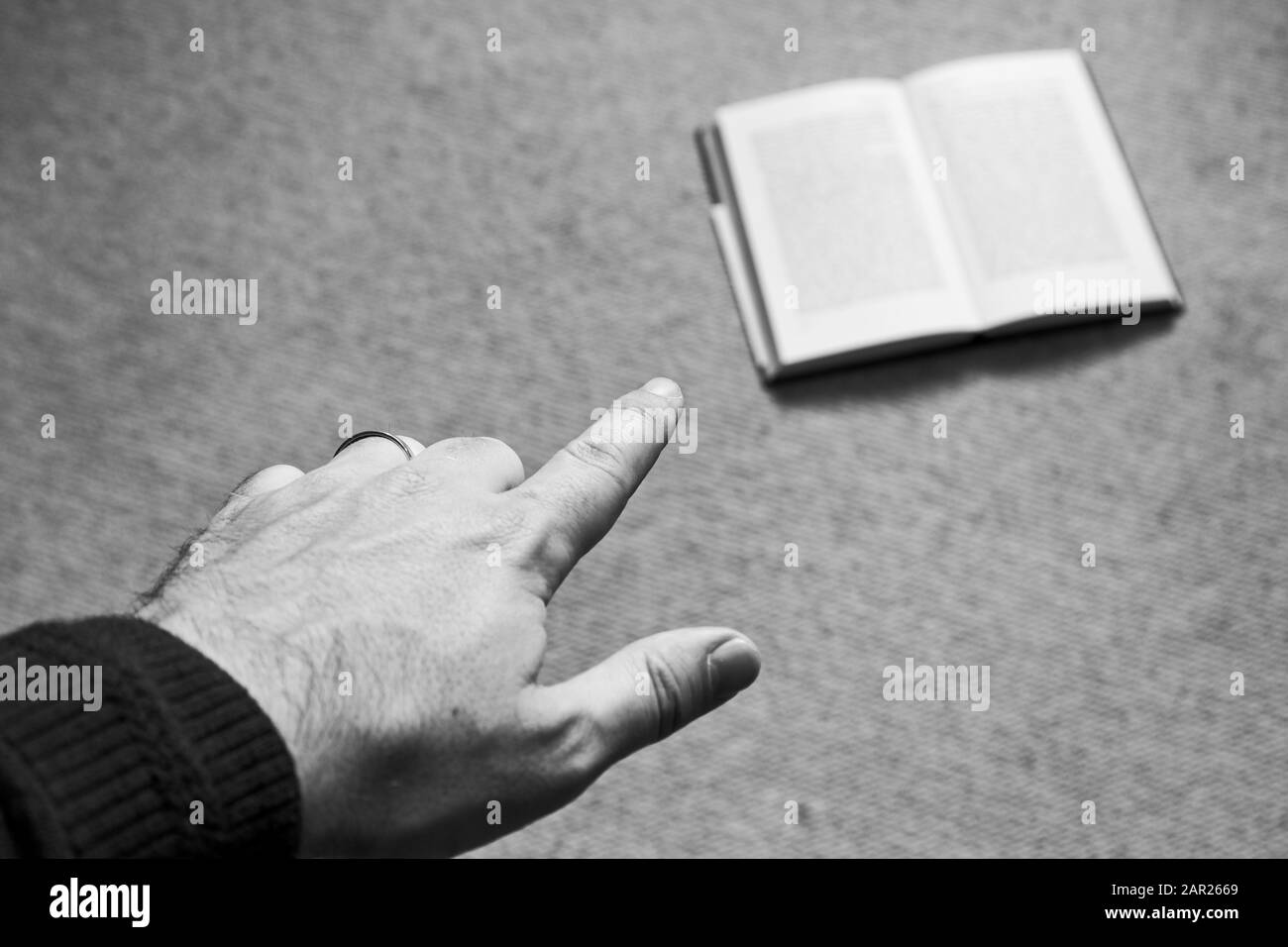 Grey scale shot of a person pointing his finger at an open book on the ...