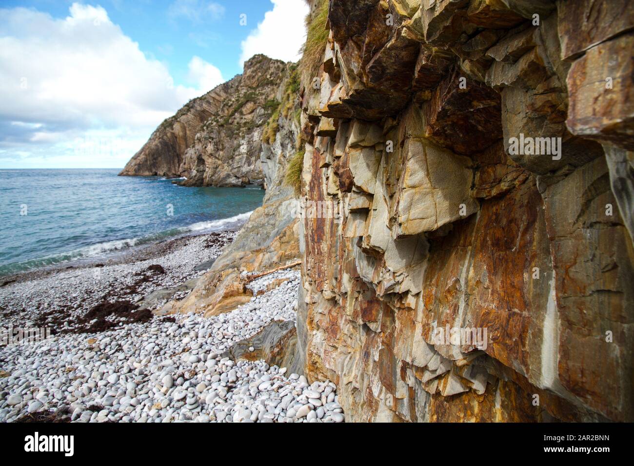 Rough colorful cliffs and wild pebble beach with view of the ocean at a ...