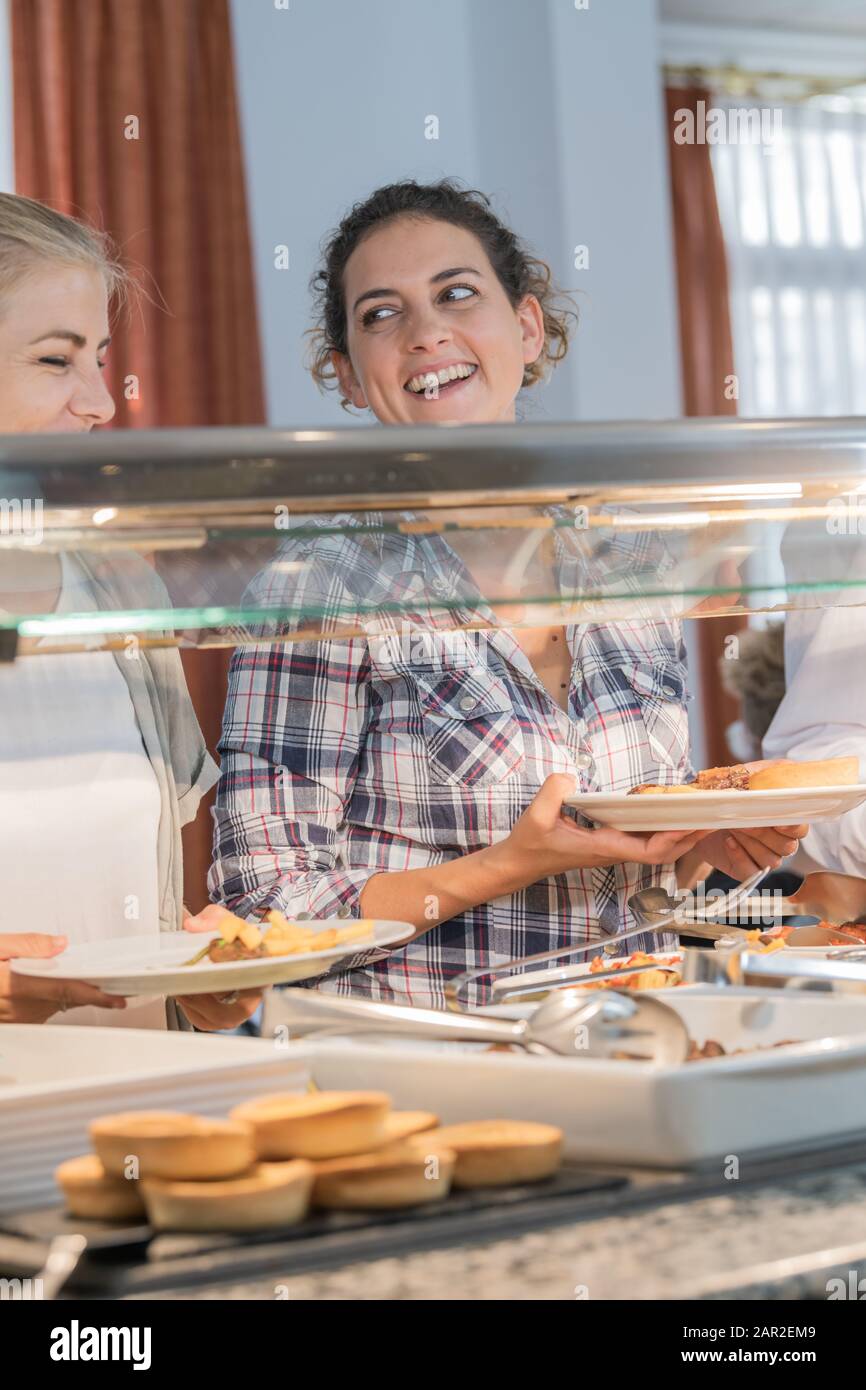 Women having fun together while getting food at a cafeteria on an out ...