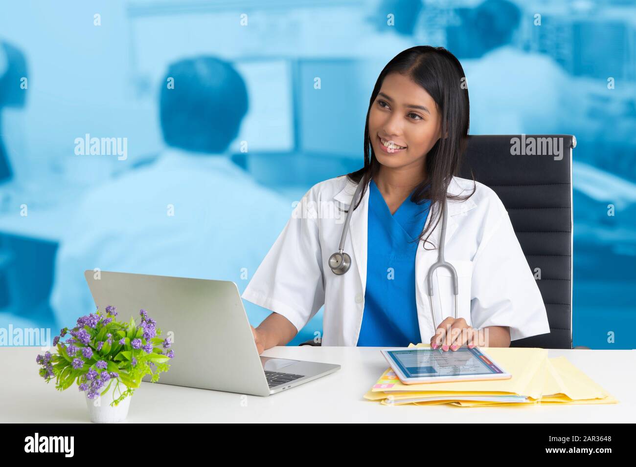 Female doctor smiled welcome while working on a notebook and computer ...